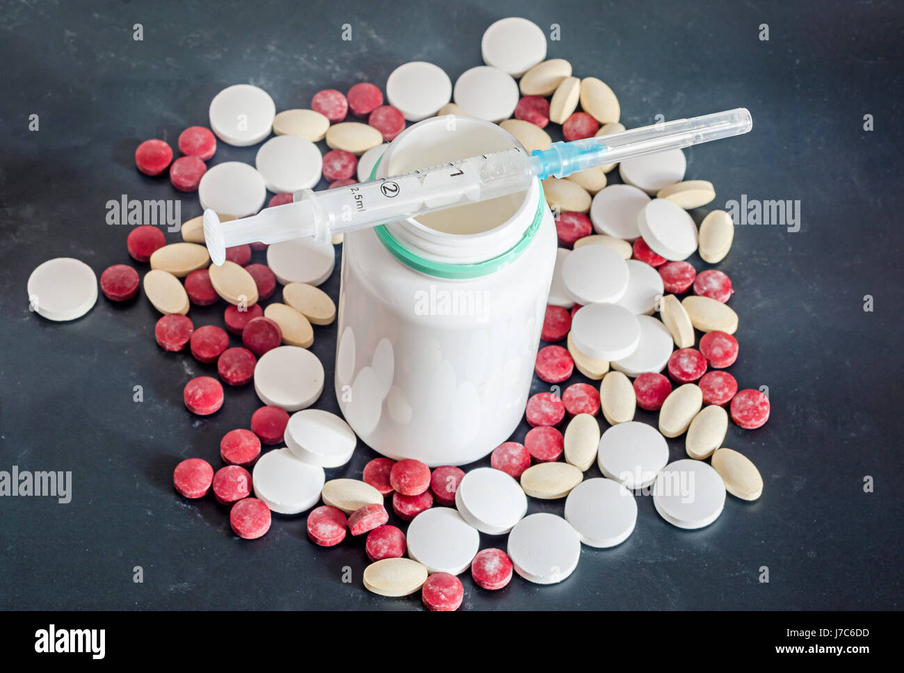 Red, white, yellow drugs pills with white open plastic bottle, syringe ...