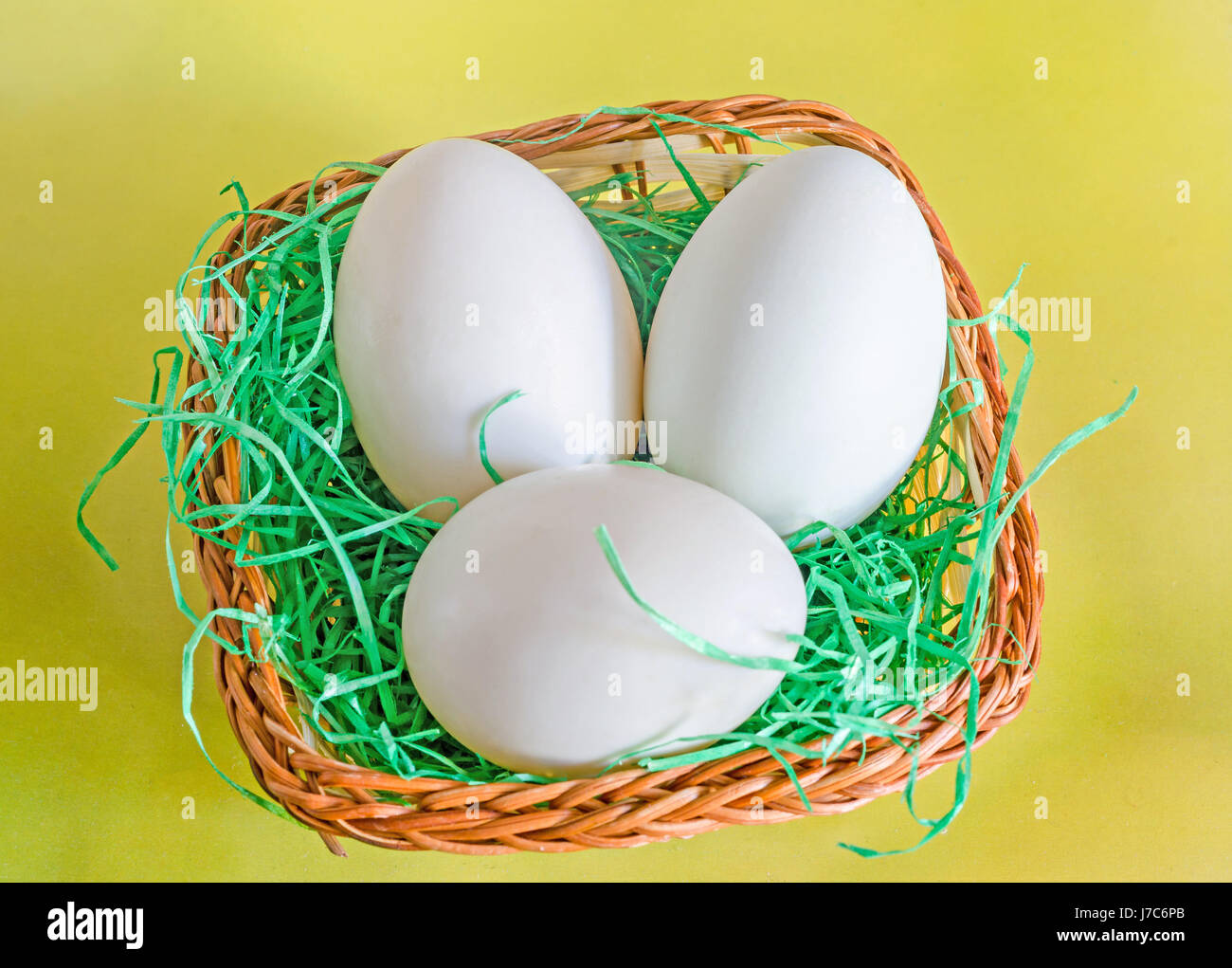 Light green duck eggs, brown basket with grass, yellow background Stock ...