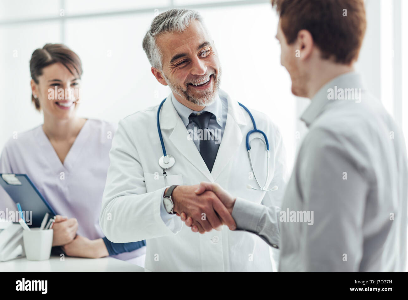 Smiling doctor at the clinic giving an handshake to his patient ...