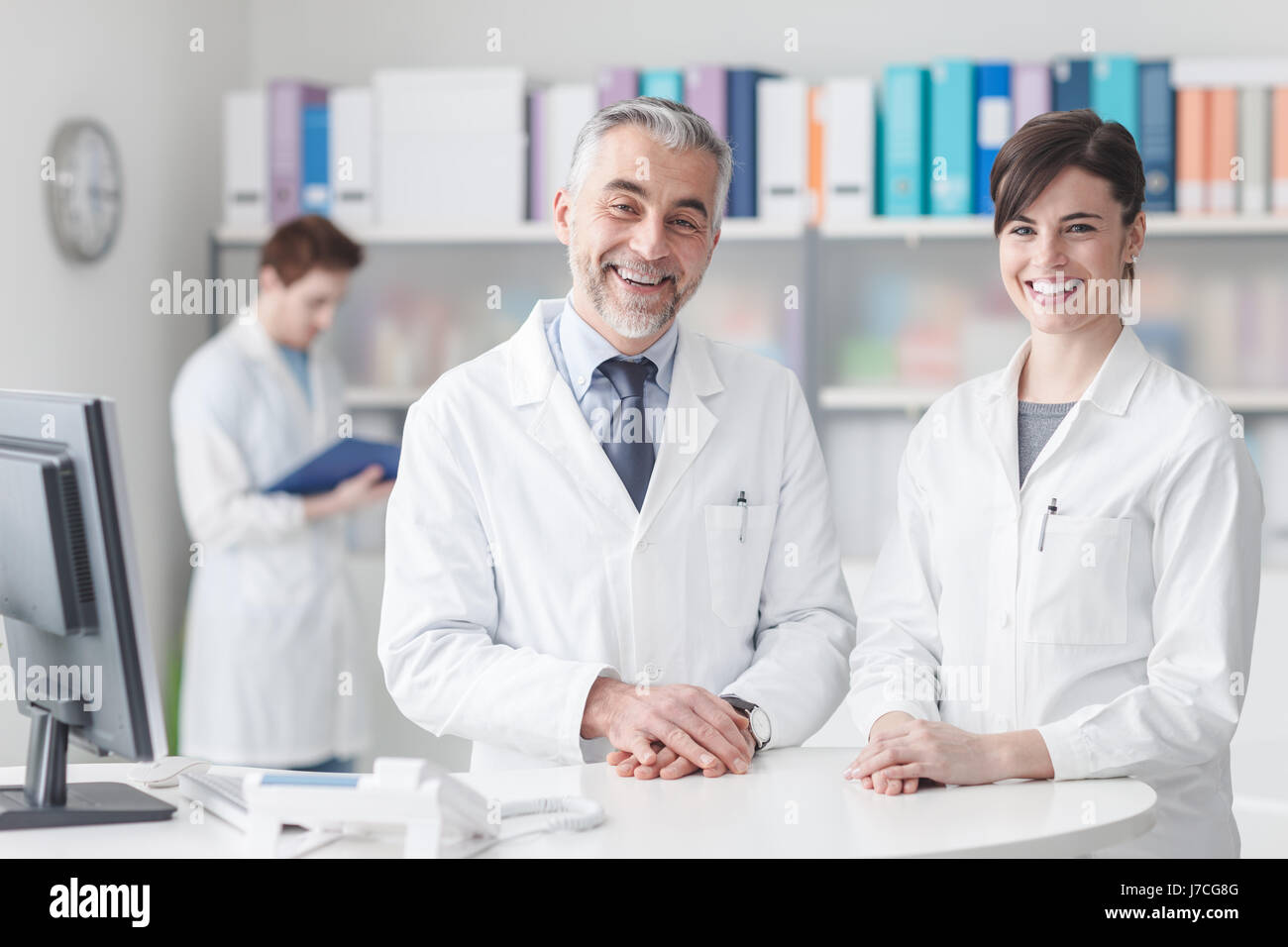 Doctor at the reception desk with his assistant, they are smiling at ...