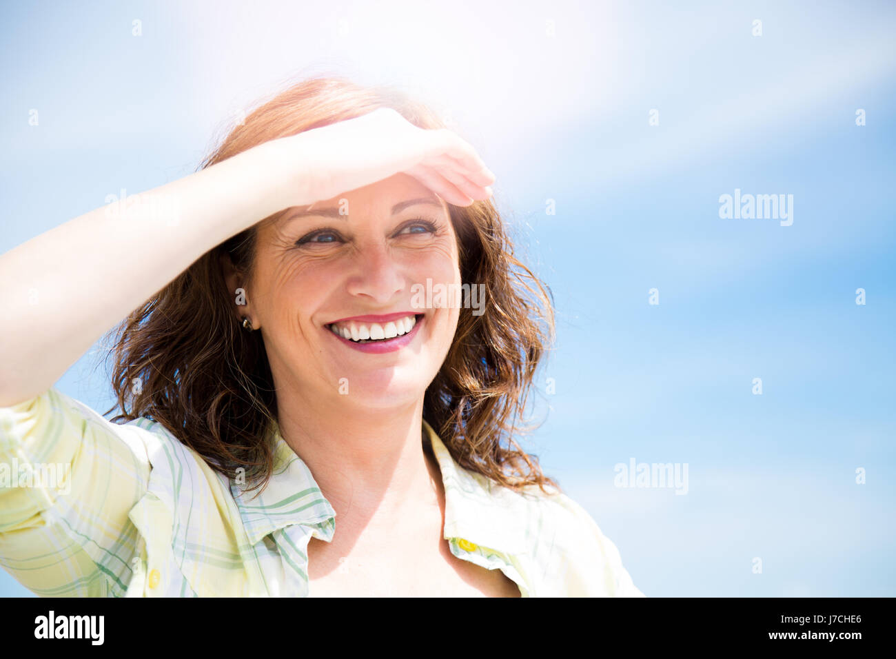Happy beautiful middle aged woman protecting from sun with hand as a ...