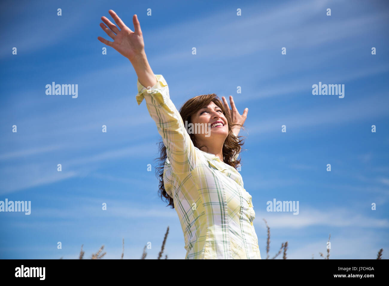 Attractive middle aged woman enjoying nature with arms raised to the ...