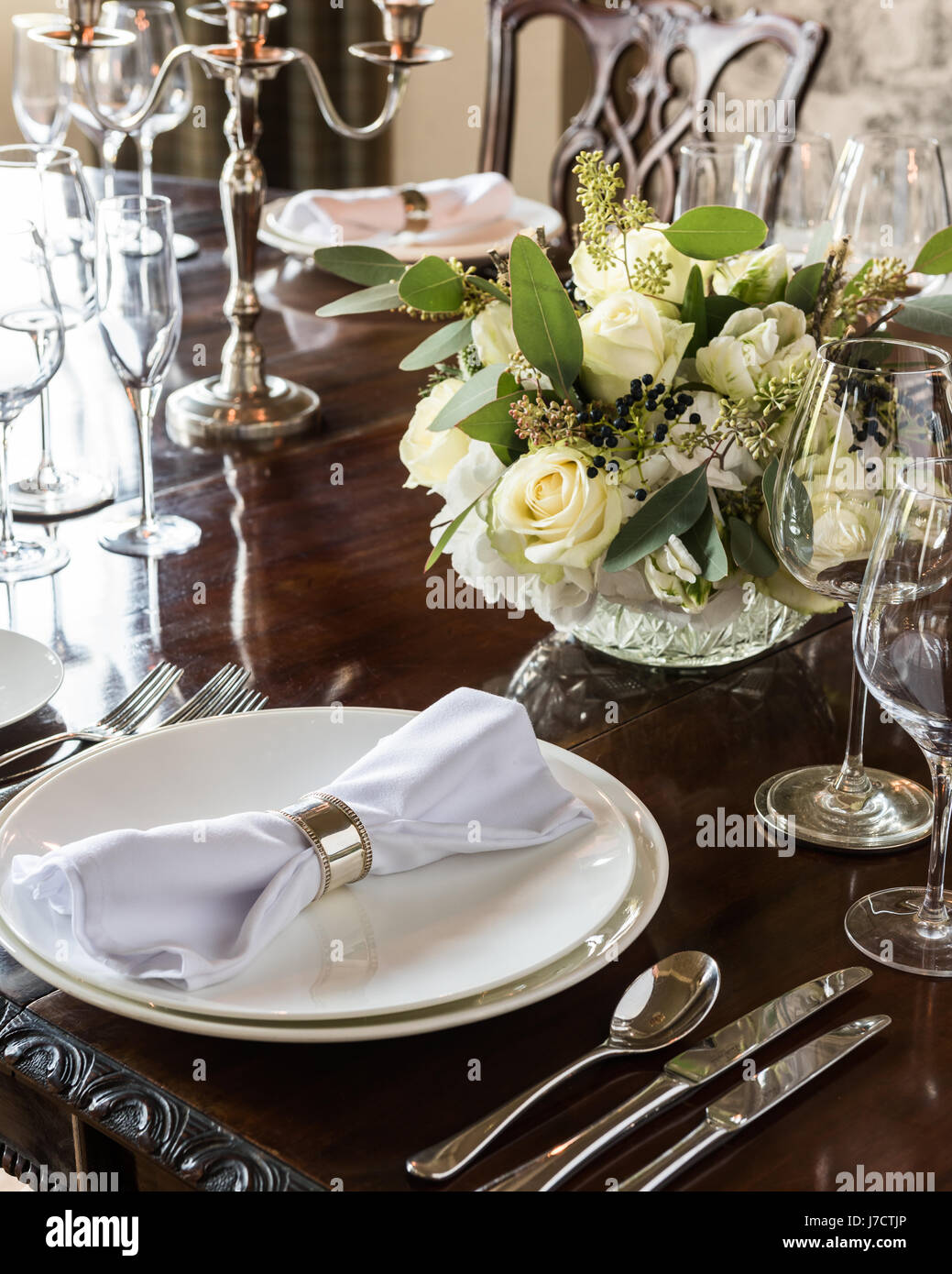 Formal dining place laid with silver cutlery and posey of white roses ...