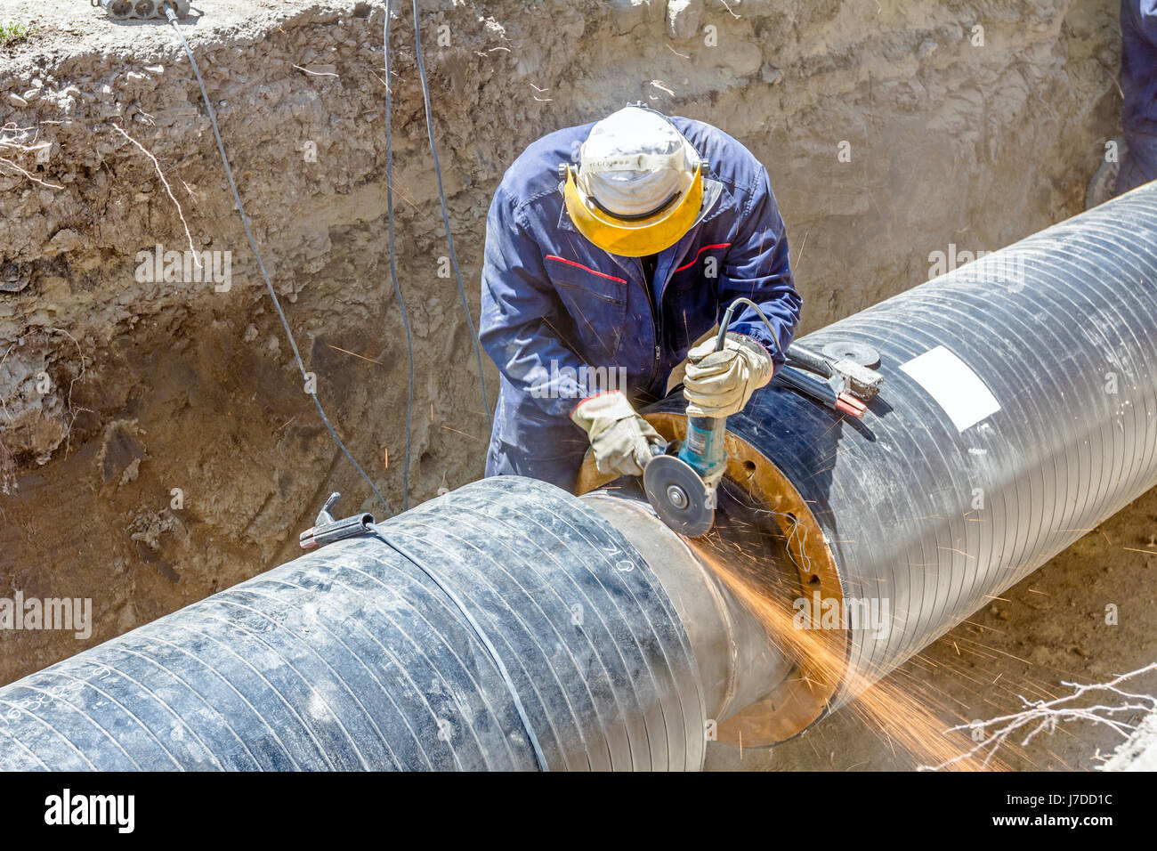 Worker is cleaning welding seam on pipeline with a grinding machine ...