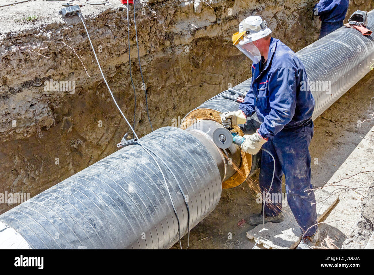 Worker is cleaning welding seam on pipeline with a grinding machine ...