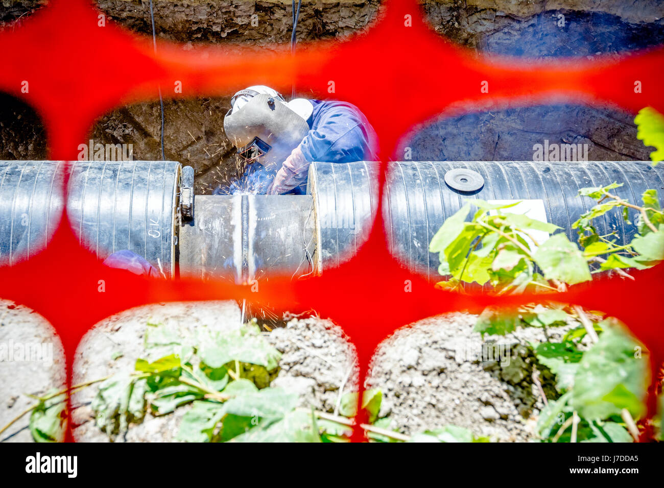 Welder is in trench arc welding pipeline. Confined space with orange ...