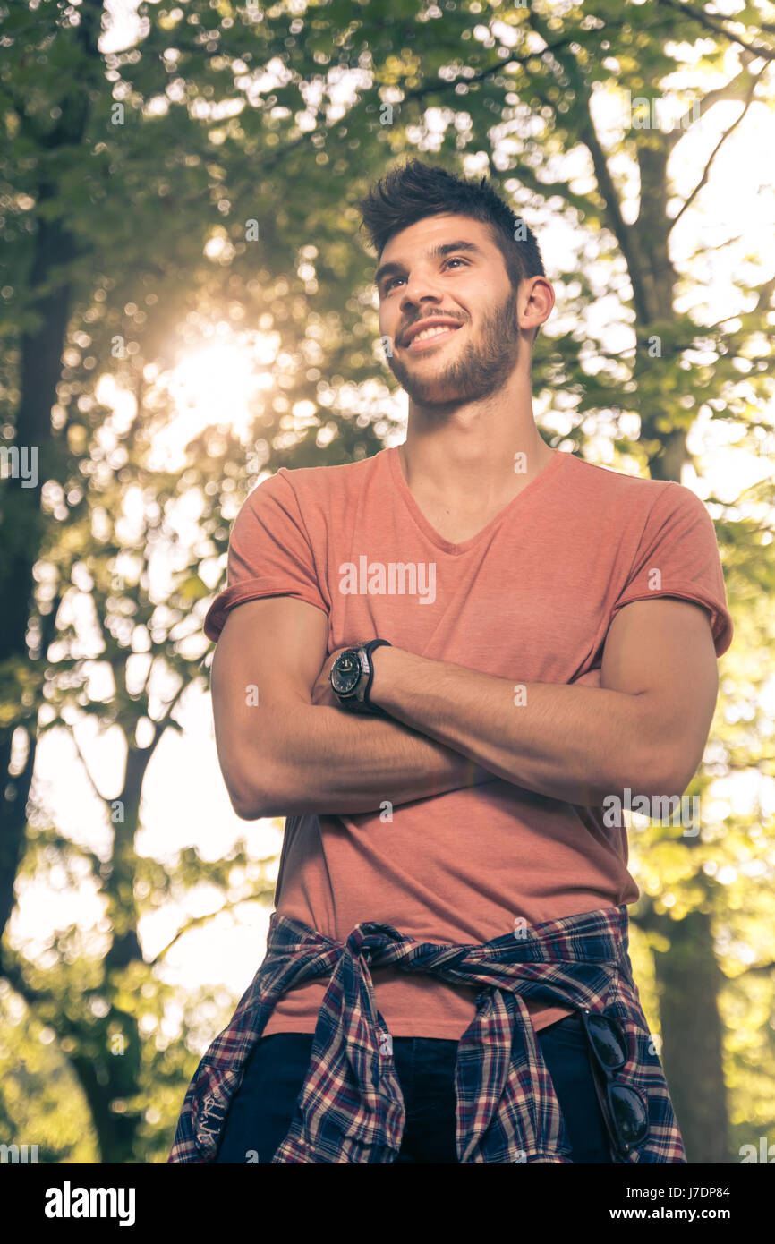 one young man, smiling, upper body shot, outdoors park nature tree ...