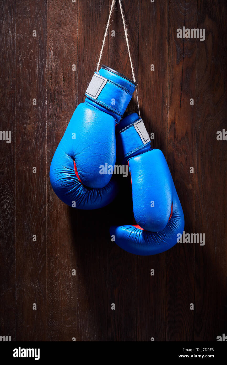 Two blue boxing gloves hanging against wooden background. Vertical ...
