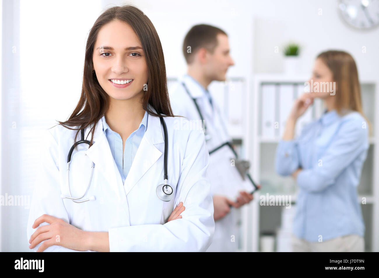 Young beautiful female doctor smiling on the background with patient in ...
