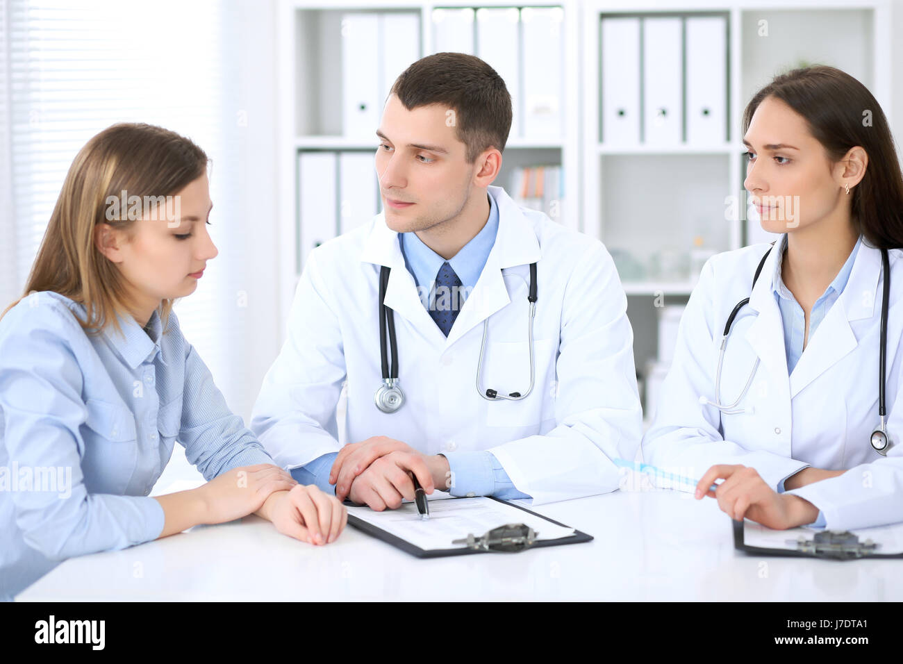 Two doctors and patient sitting at the table in medical cabinet Stock ...
