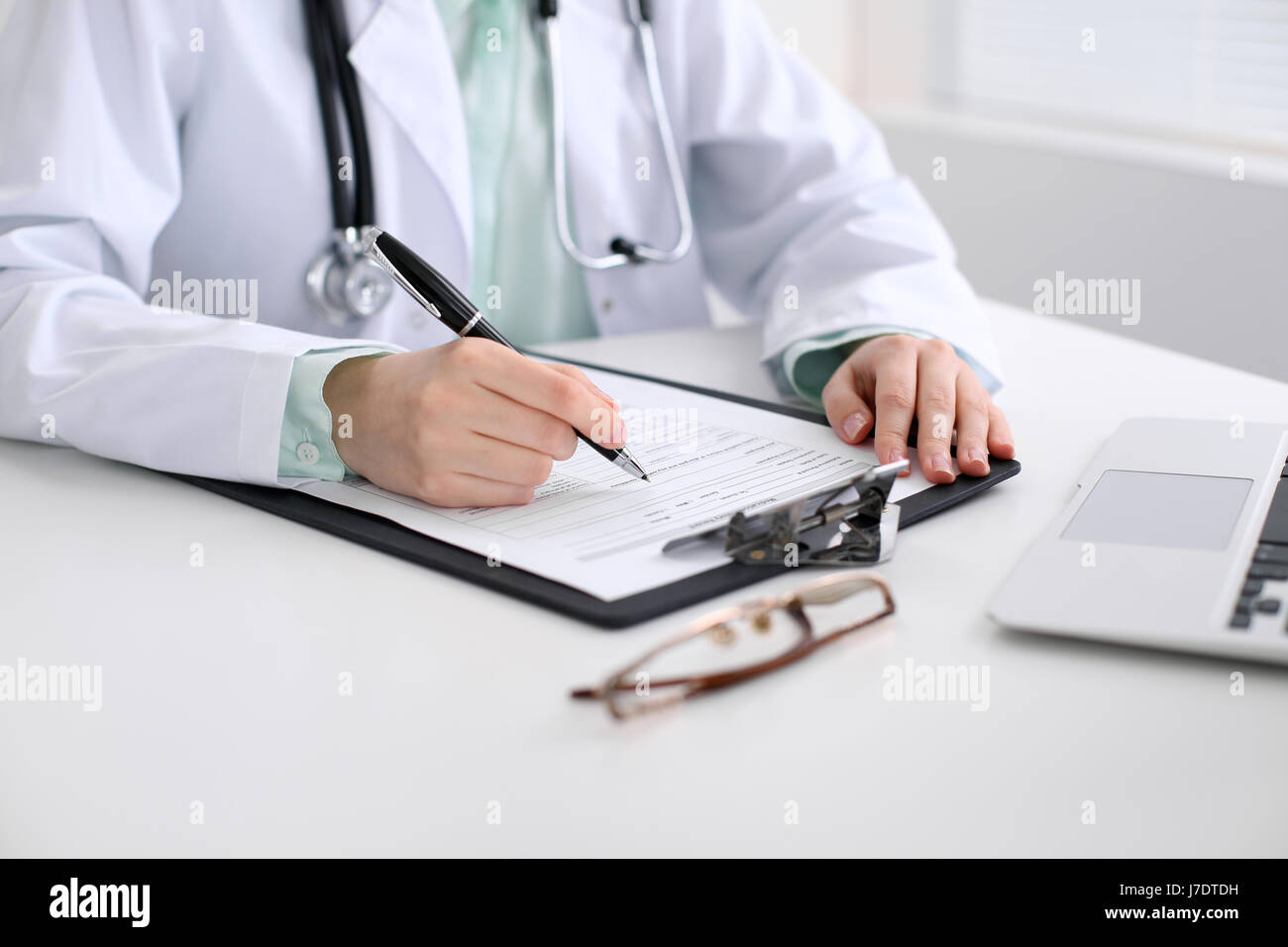 Close-up of a female doctor filling out application form , sitting at ...