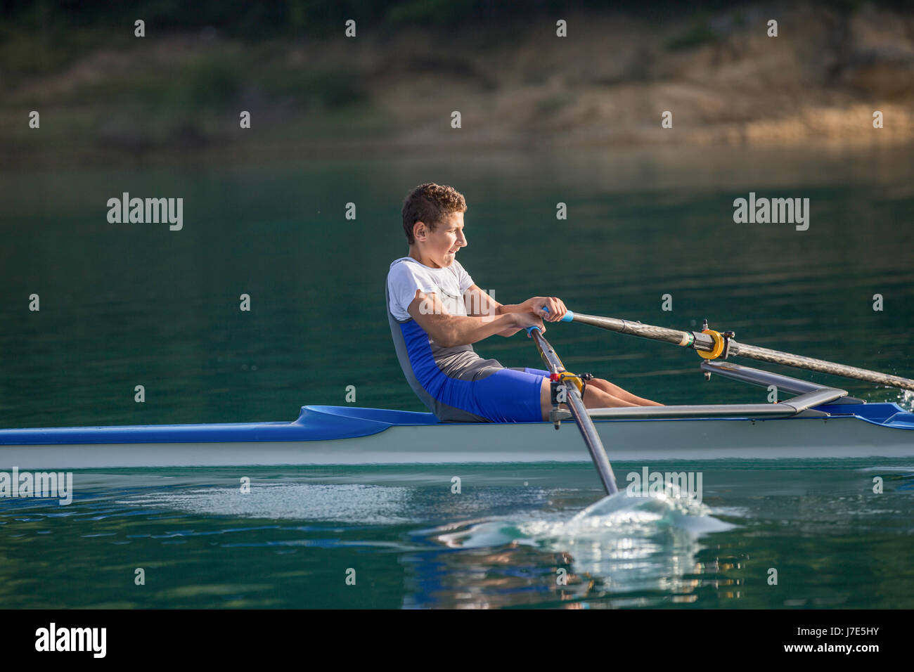 A Young single scull rowing competitor paddles on the tranquil lake ...