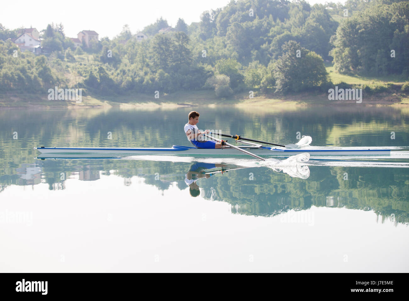 A Young single scull rowing competitor paddles on the tranquil lake ...