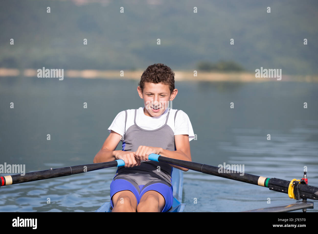 A Young single scull rowing competitor paddles on the tranquil lake ...