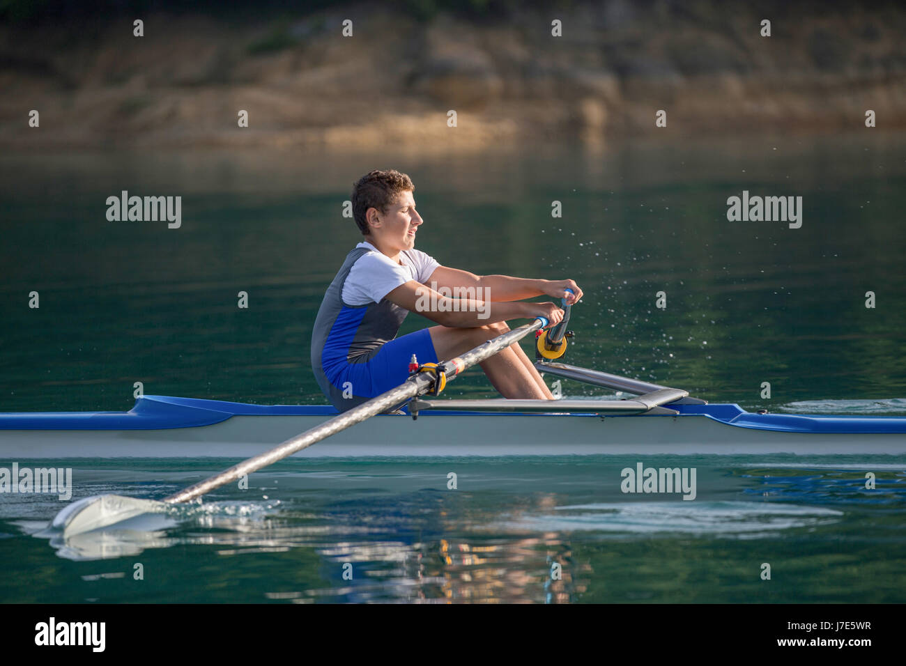 A Young single scull rowing competitor paddles on the tranquil lake ...