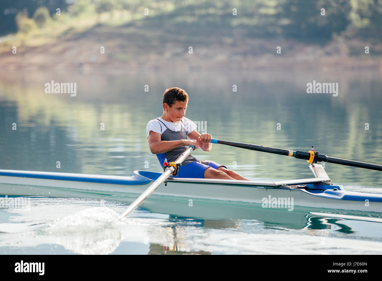 A Young single scull rowing competitor paddles on the tranquil lake ...