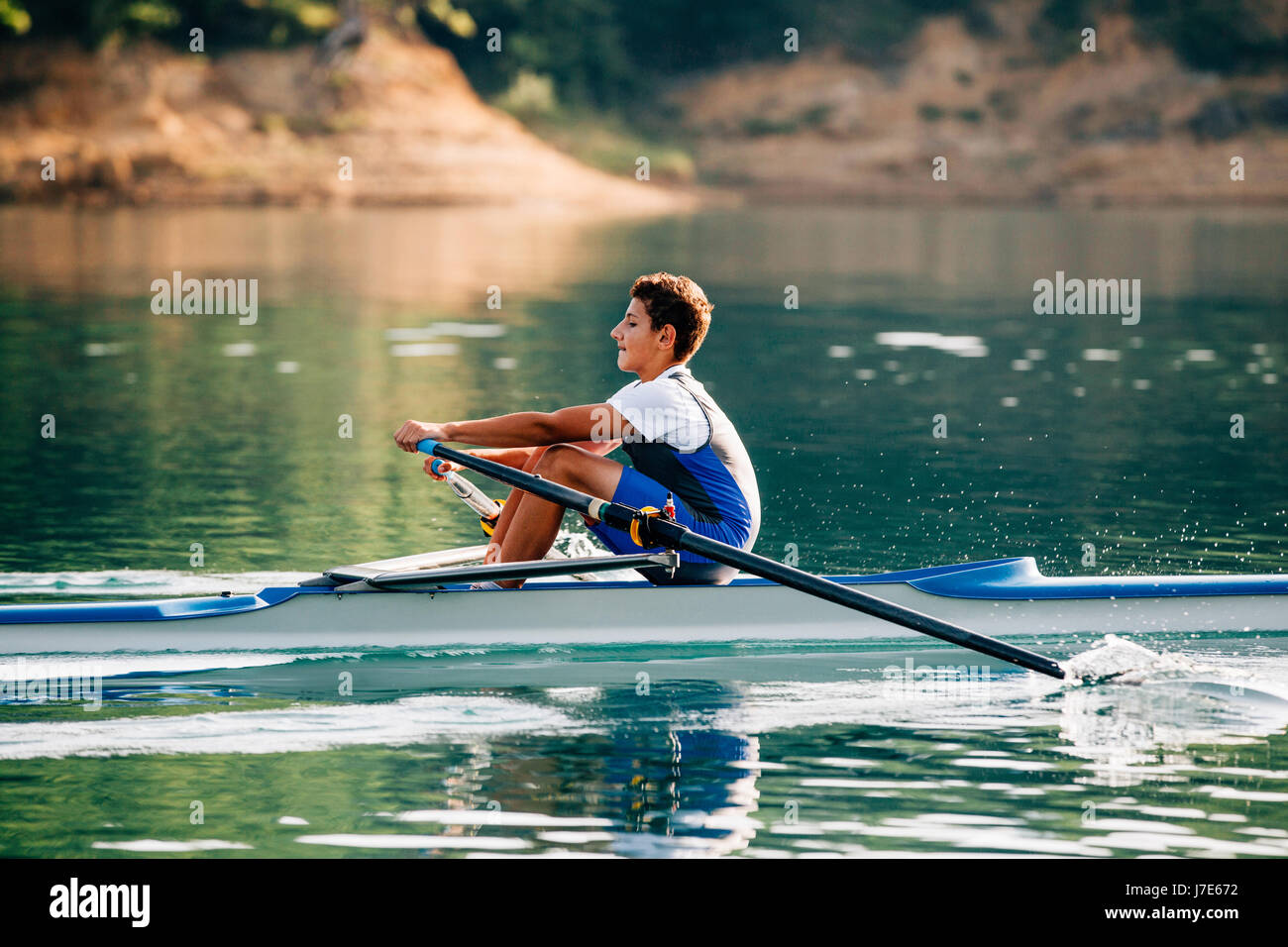 A Young single scull rowing competitor paddles on the tranquil lake ...