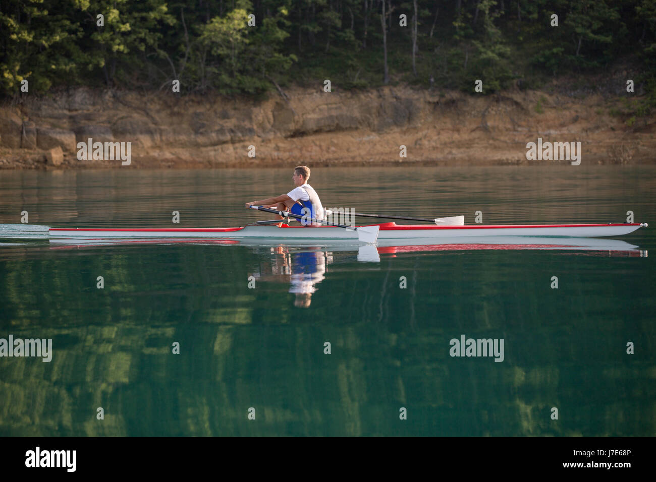 A Young single scull rowing competitor paddles on the tranquil lake ...
