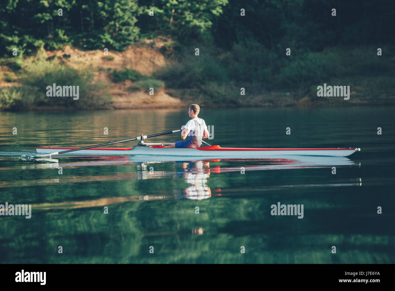 A Young single scull rowing competitor paddles on the tranquil lake ...