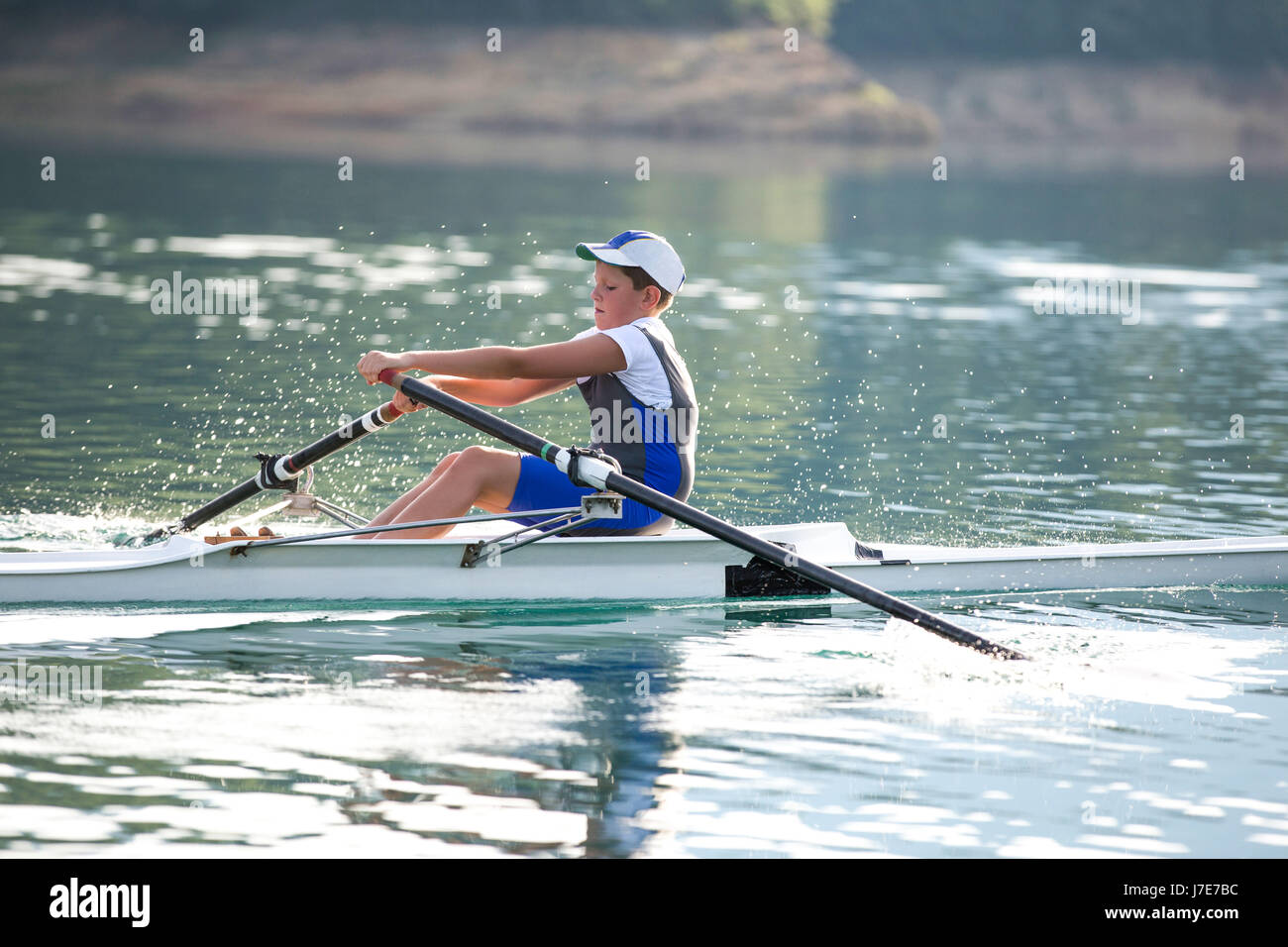 A Young single scull rowing competitor paddles on the tranquil lake ...