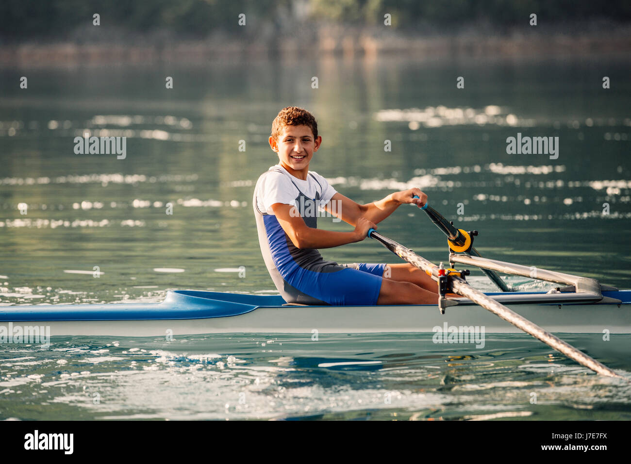 A Young single scull rowing competitor paddles on the tranquil lake ...