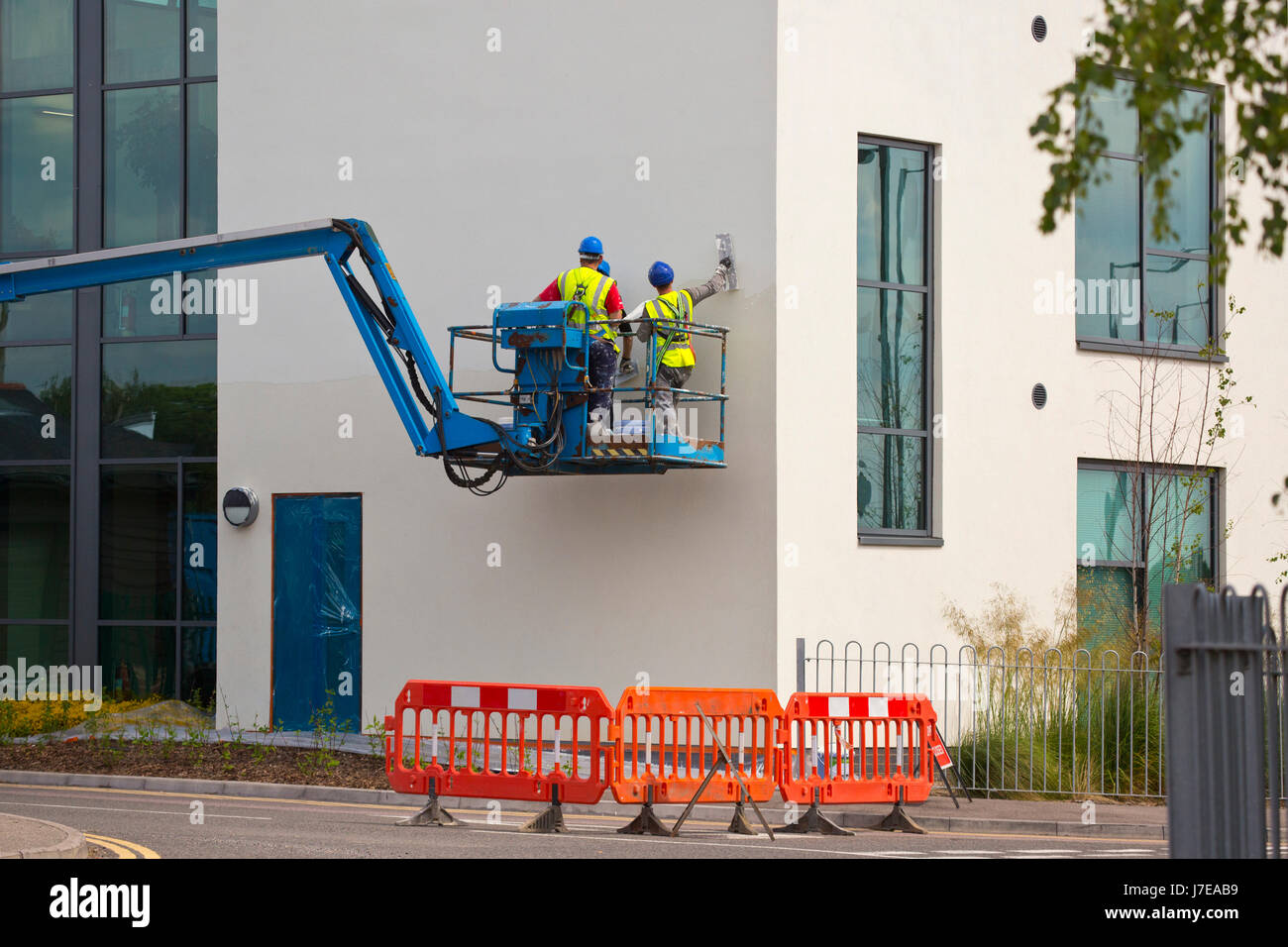 three plasterers working on a new office building from a lift platform ...