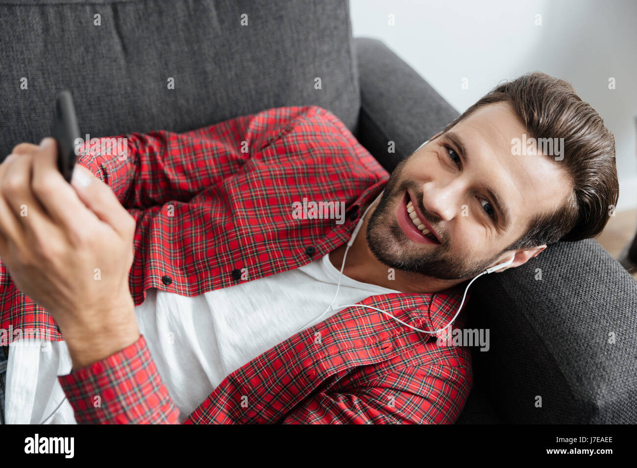 Image of cheerful young man lies on sofa indoors at home while ...