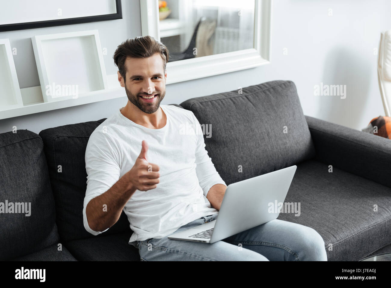 Picture of cheerful young man sitting indoors at home while using ...