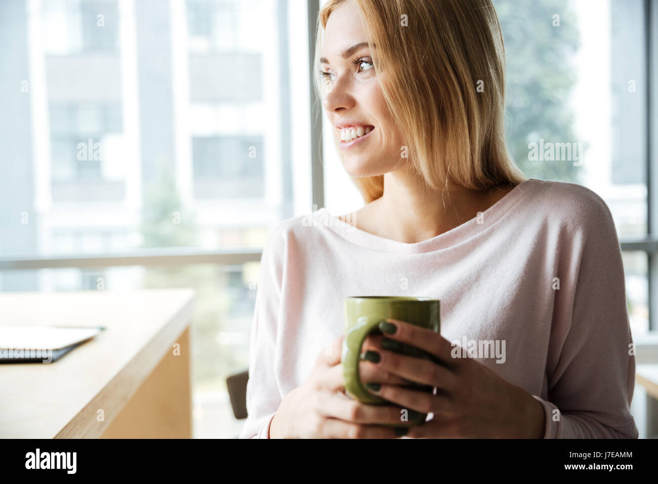 Picture of young happy lady in office coworking drinking tea. Looking ...