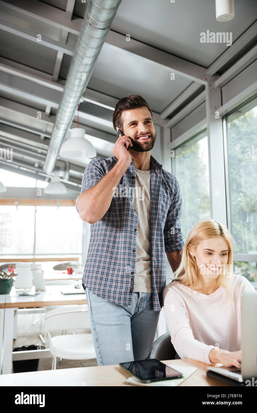 Picture of young happy two colleagues in office coworking while using ...