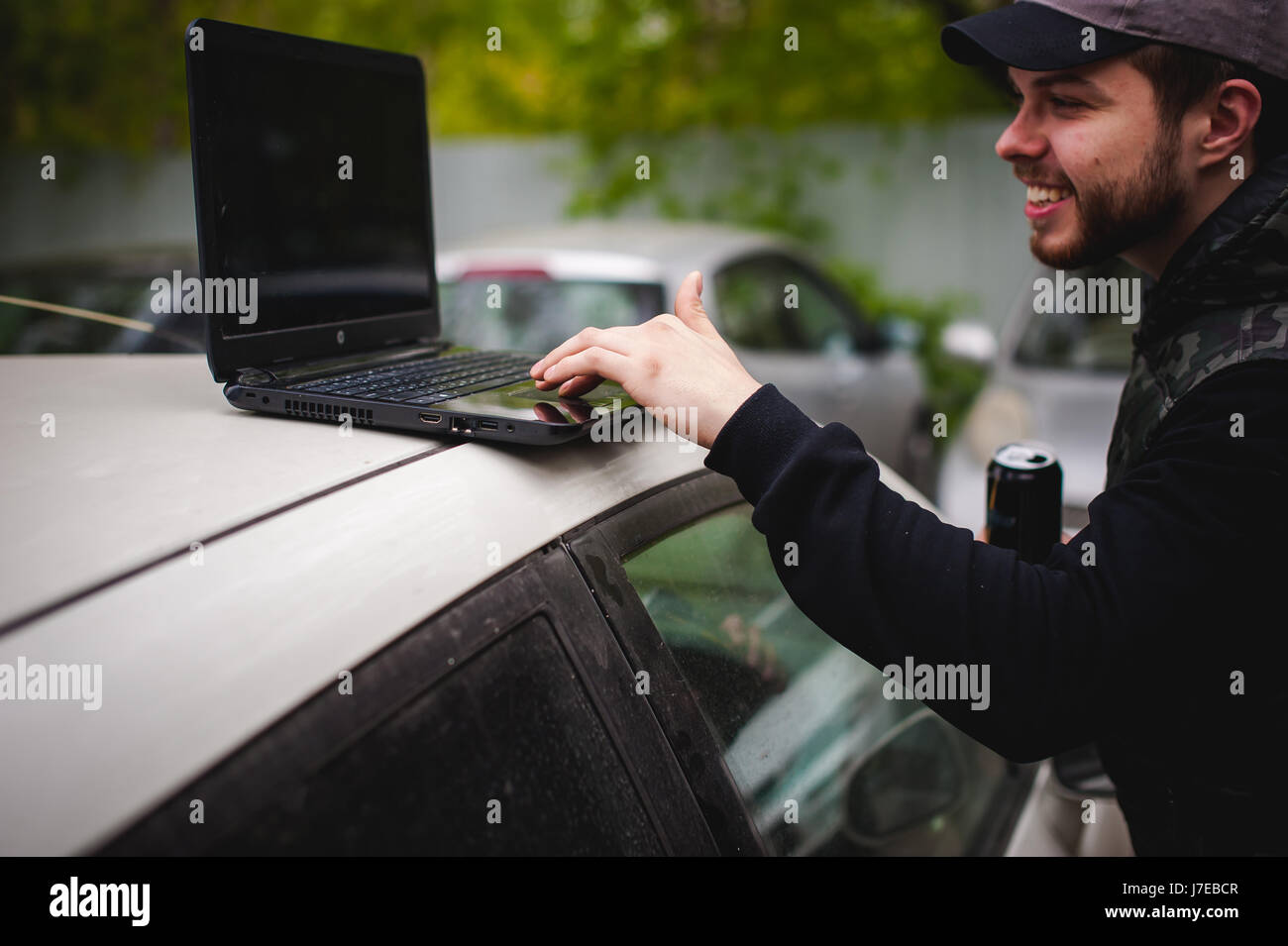 man with a laptop in parking lot in yard near car is doing ...