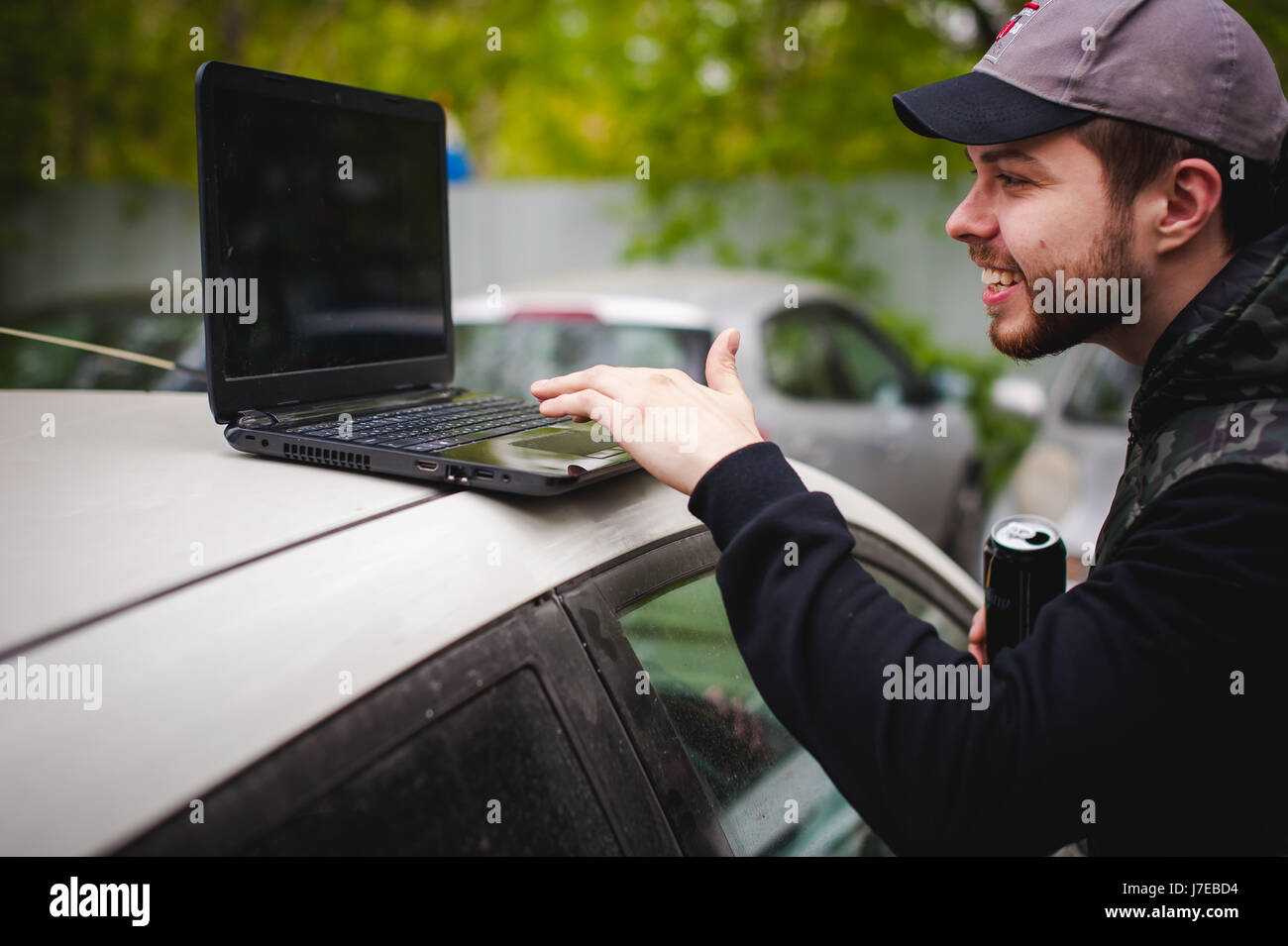 man with a laptop in parking lot in yard near car is doing ...