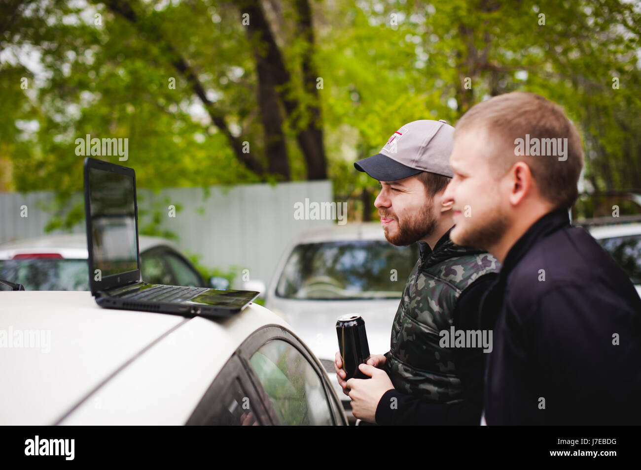 man with a laptop in parking lot in yard near car is doing ...