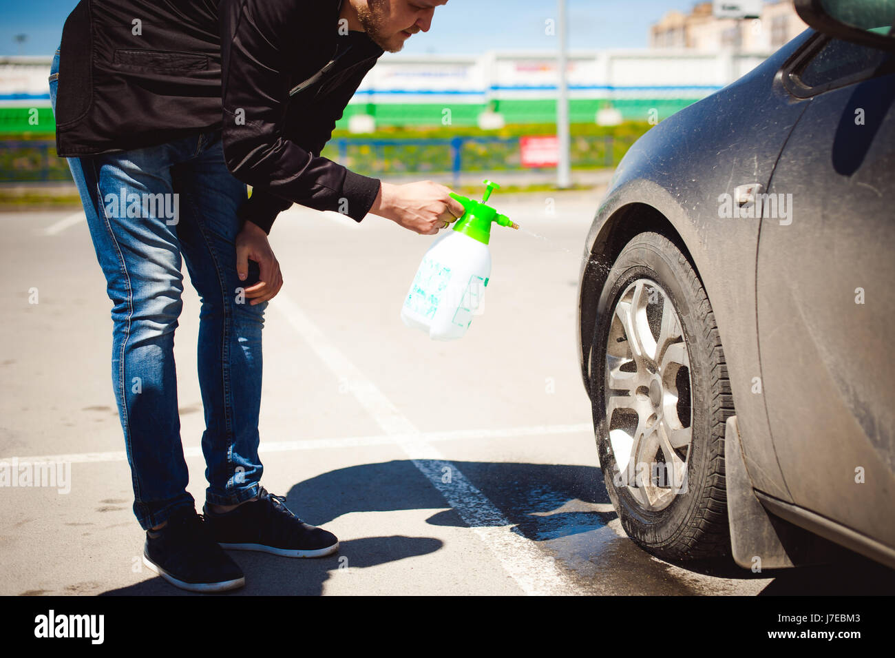 young bearded man washes his car's wheel rims, spraying water from ...