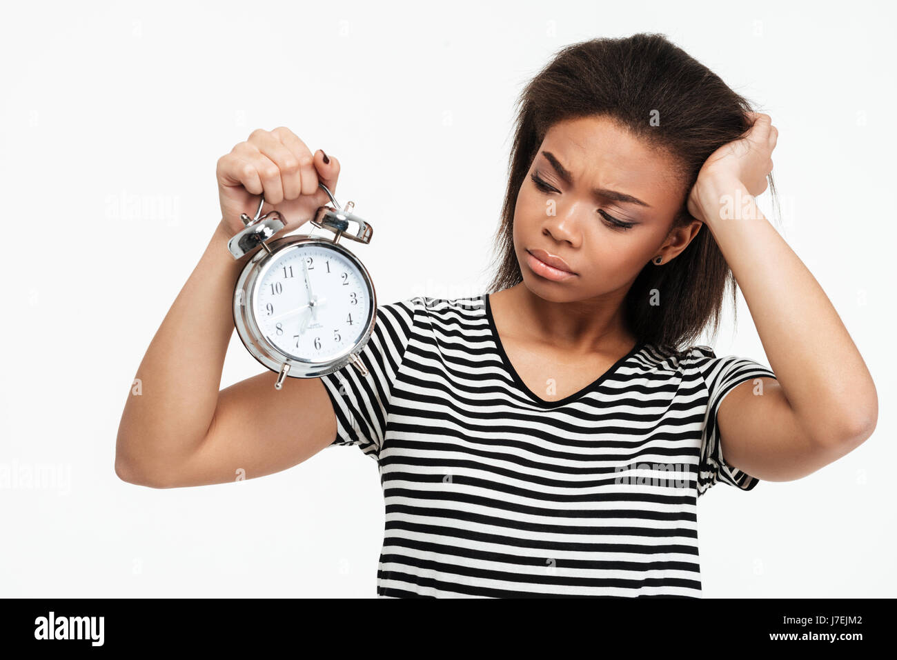 Portrait of an upset frustrated african girl looking at alarm clock ...