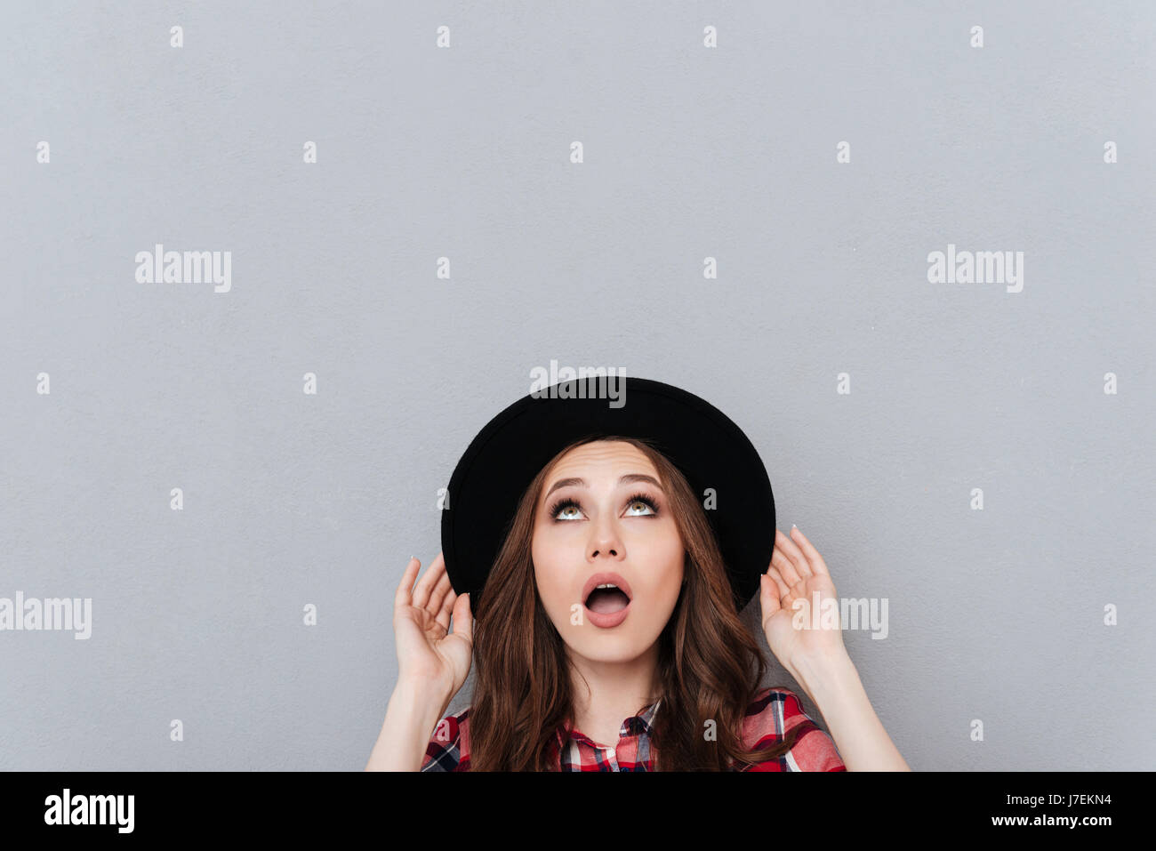 Portrait of a shocked young woman in hat looking up at copyspace ...