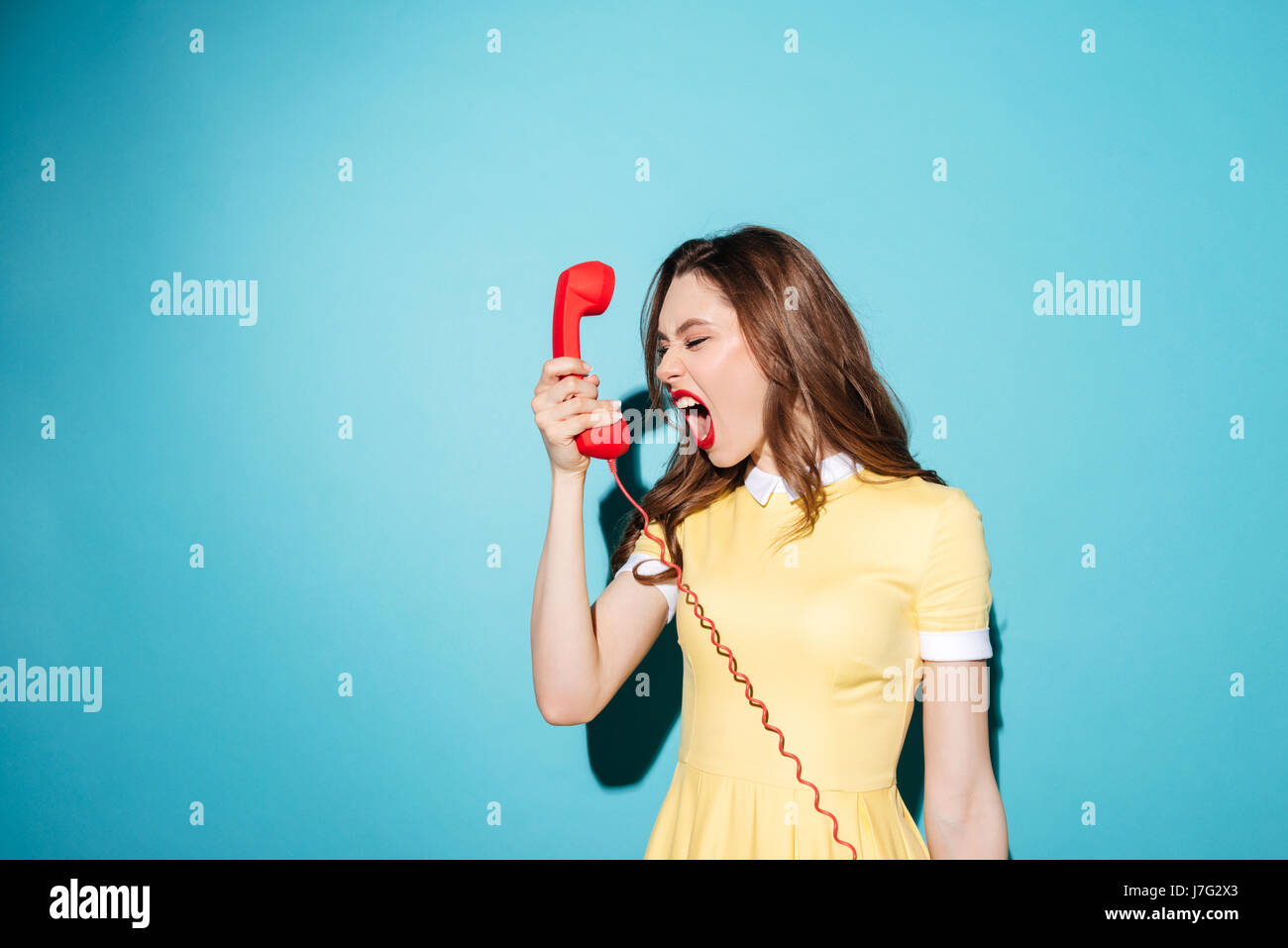 Portrait of an angry furious girl in dress screaming at retro telephone ...