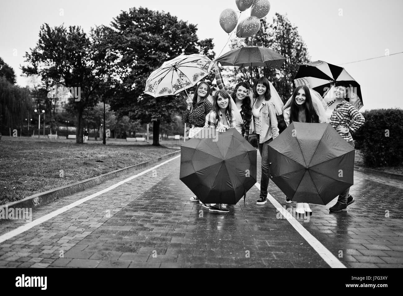 Group of six girls having fun at hen party, with umbrella under rain ...