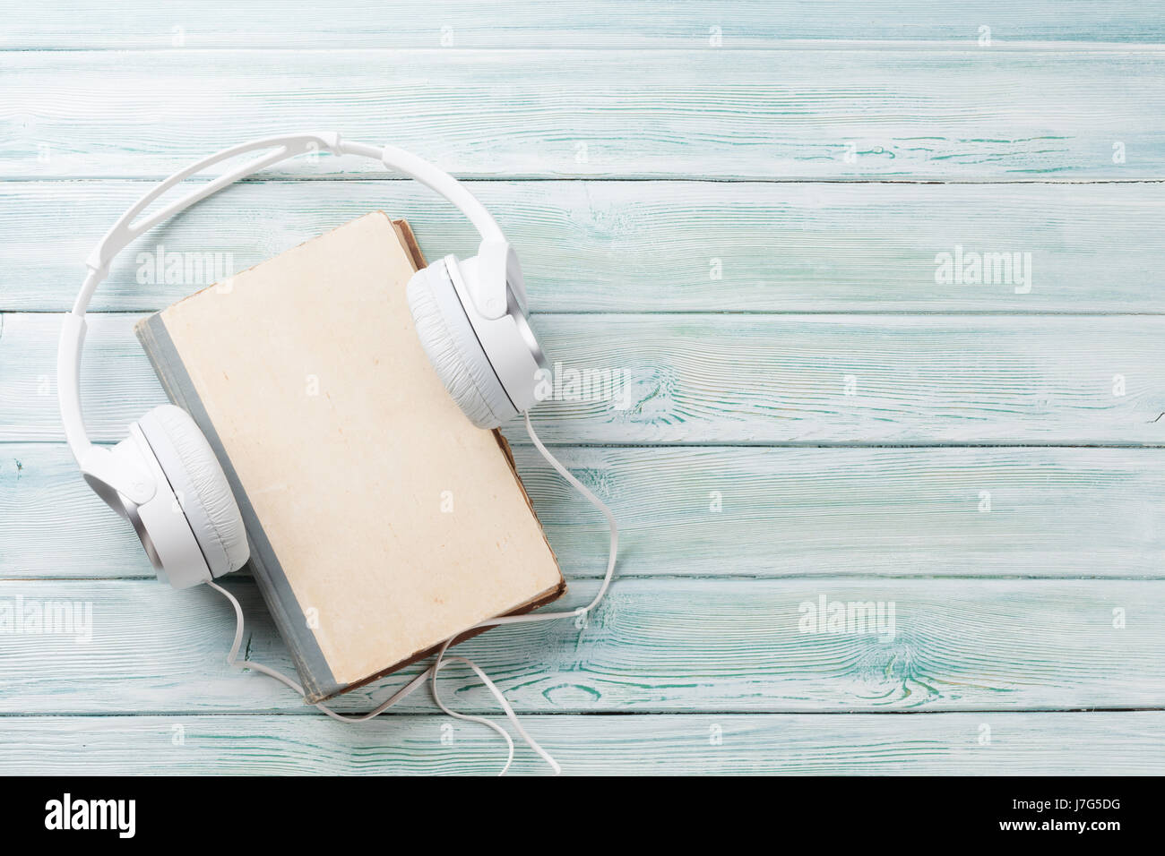 Audio book concept. Headphones and old book over wooden table. Top view ...