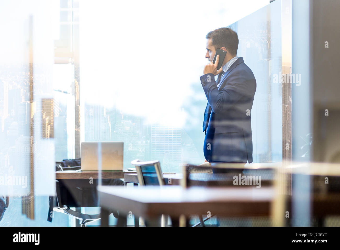Businessman talking on a mobile phone while looking through window in ...