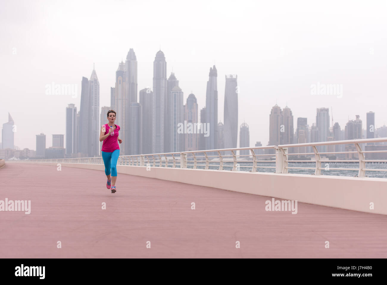 very active young beautiful woman busy running on the promenade along ...