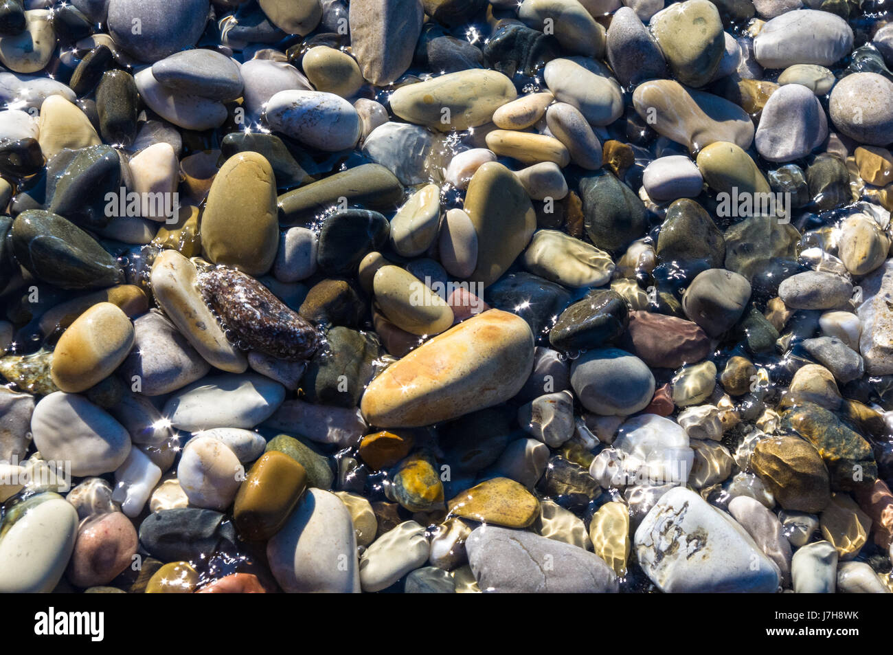 sea pebble beach with multicoloured stones, transparent waves with foam ...