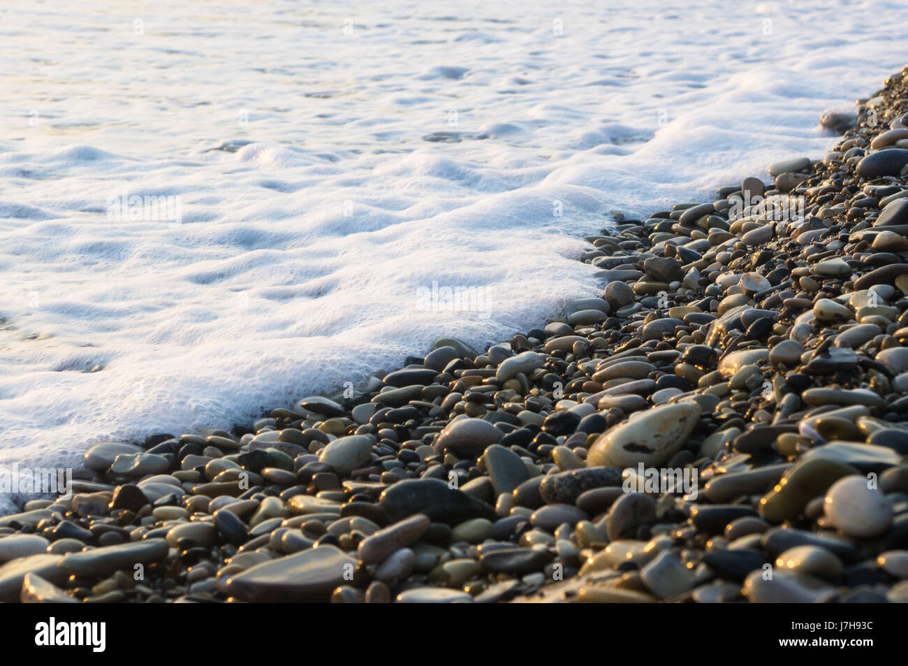 sea pebble beach with multicoloured stones, transparent waves with foam ...