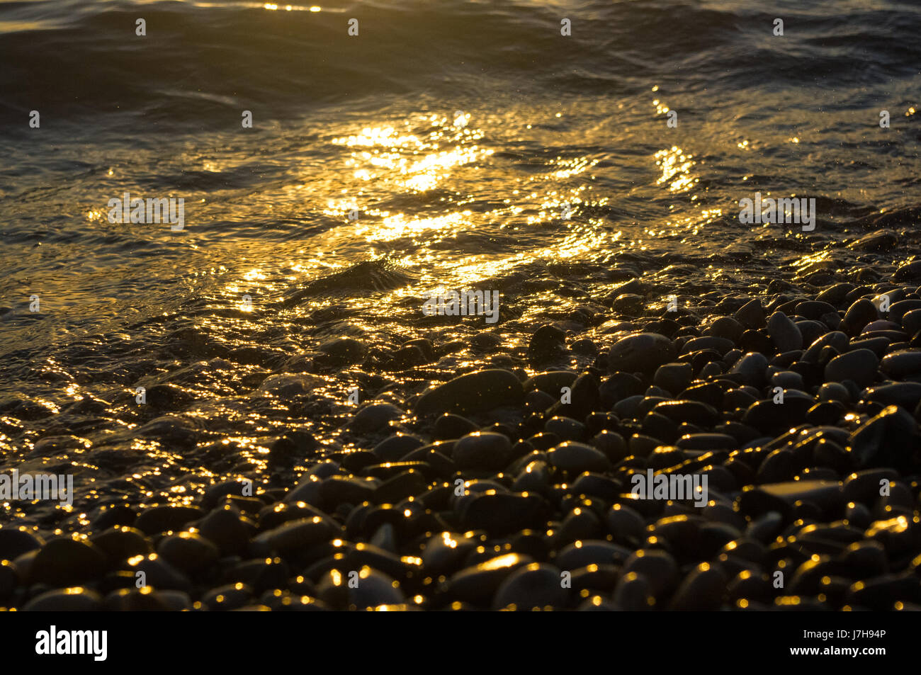 sea pebble beach with multicoloured stones, transparent waves with foam ...