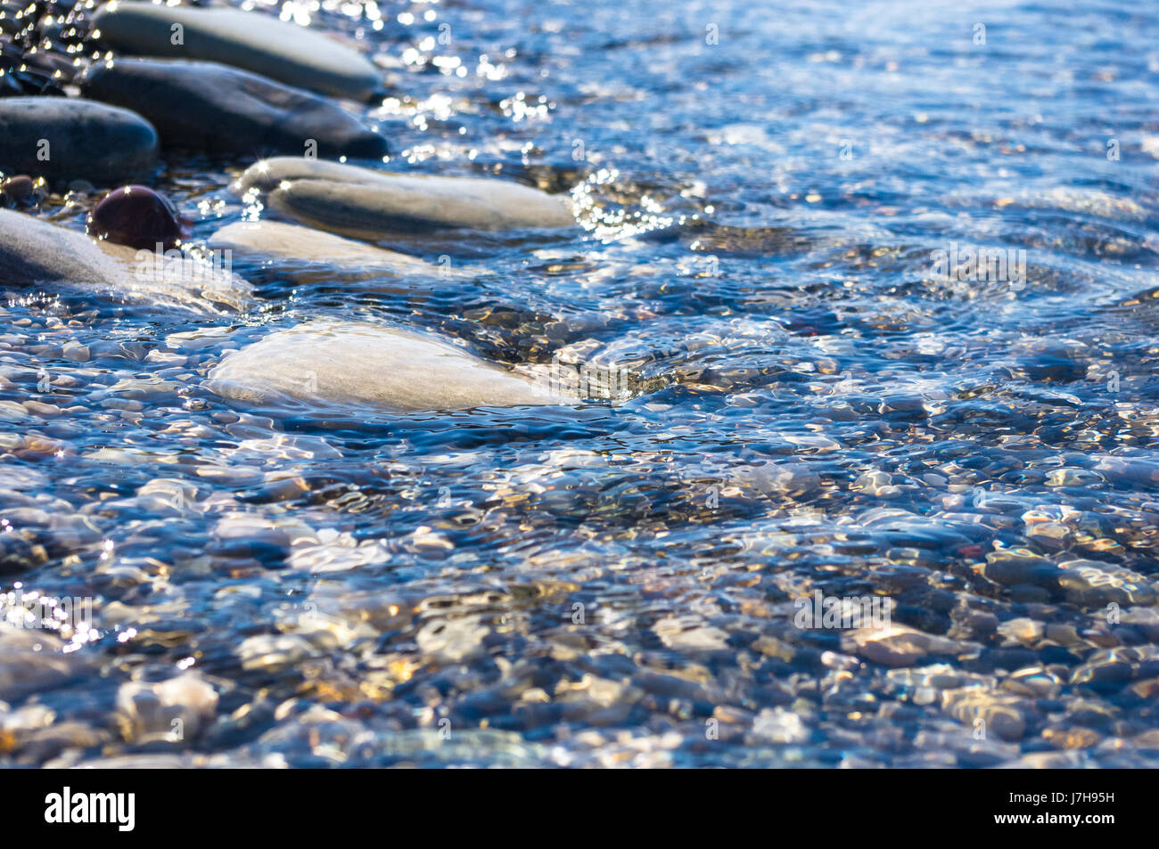 sea pebble beach with multicoloured stones, transparent waves with foam ...