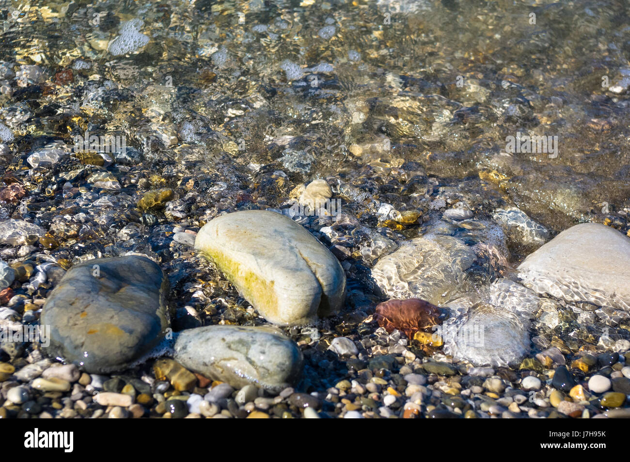 sea pebble beach with multicoloured stones, transparent waves with foam ...