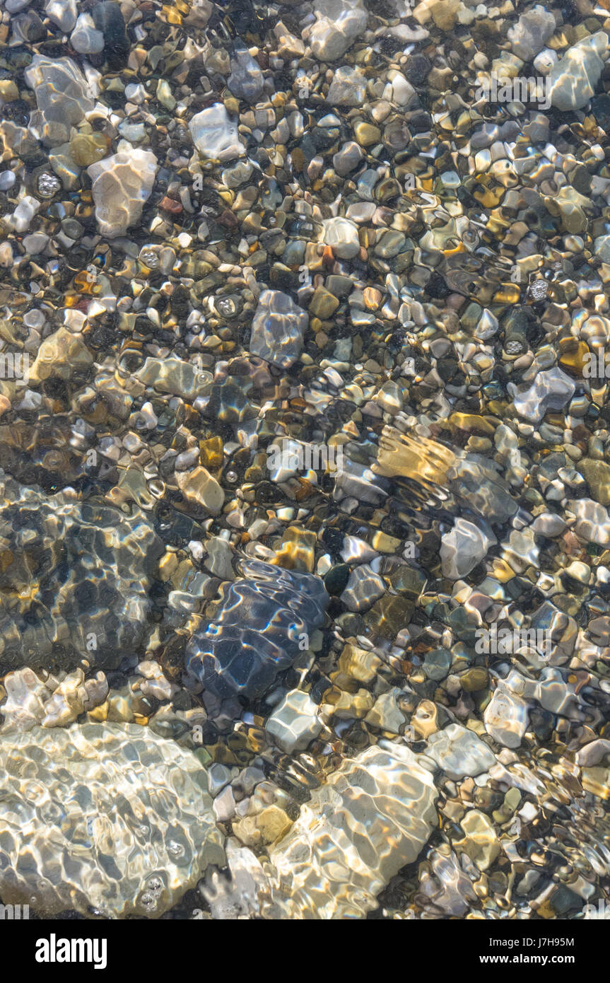 sea pebble beach with multicoloured stones, transparent waves with foam ...