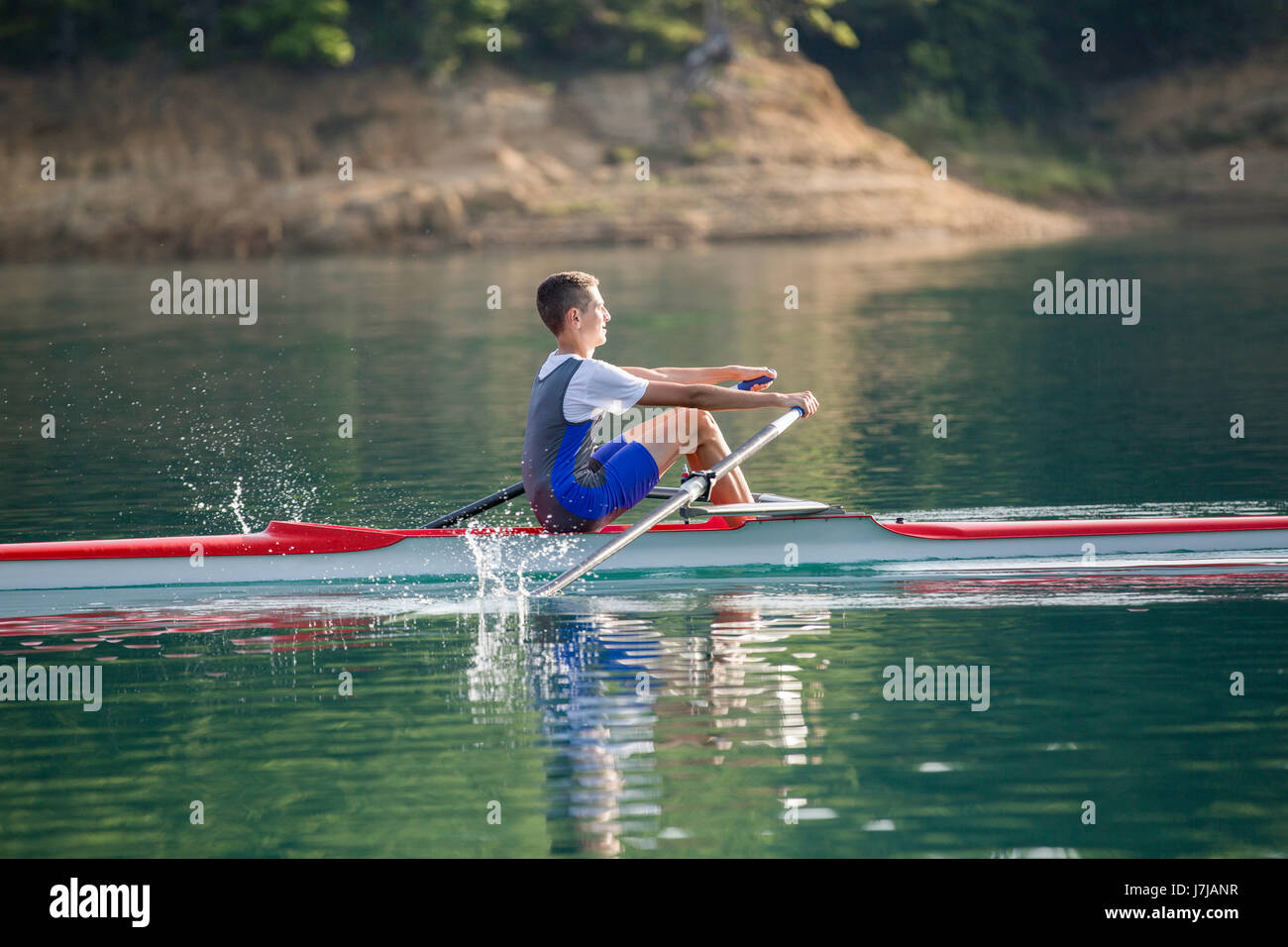 A Young single scull rowing competitor paddles on the tranquil lake ...