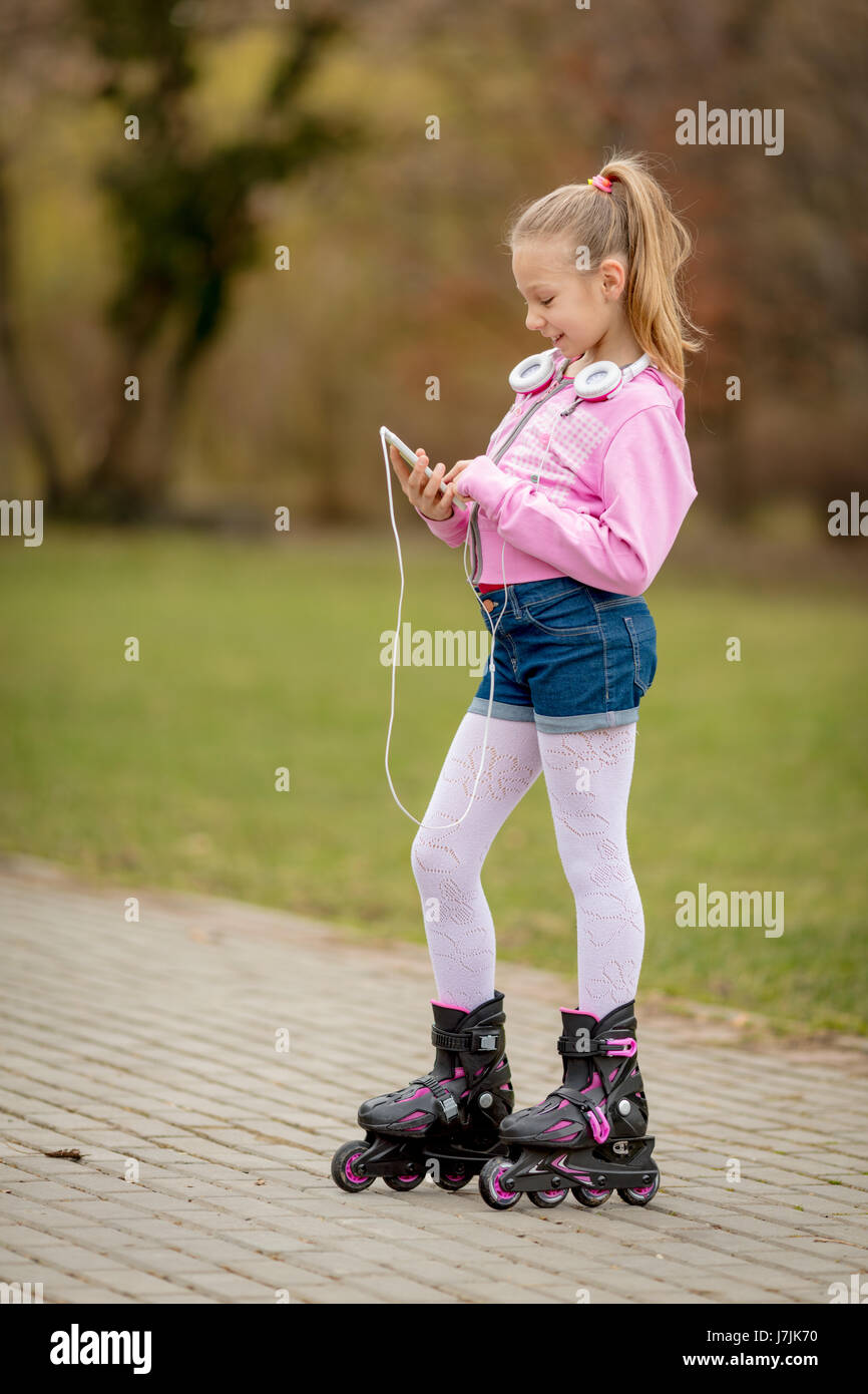 Beautiful smiling little girl inline skating through the park and using ...