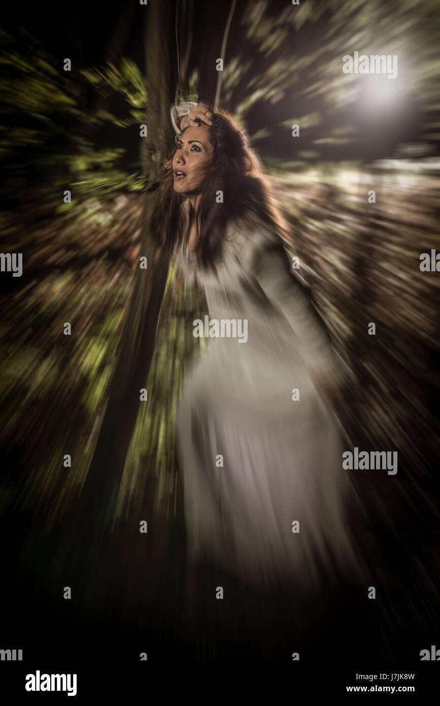 Young scared woman walking through the forest at night in white dress ...